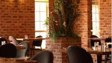 Interior de restaurante com paredes de tijolo, teto de madeira e mesas com cadeiras.