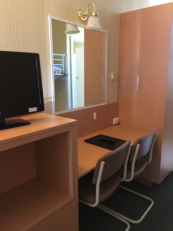Quarto compacto com escrivaninha, duas cadeiras, monitor de computador, espelho e luminária.