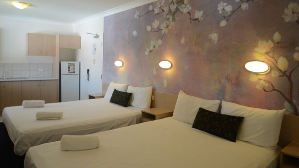 Quarto de hotel com duas camas, uma cozinha compacta e uma parede com um mural floral.