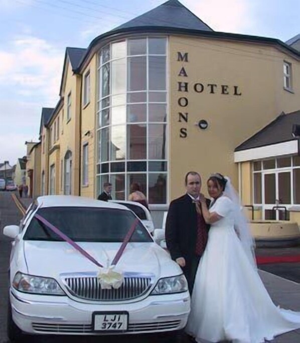 Um casal de noivos em frente a um edifício com uma placa que diz 'MAHONS HOTEL'.