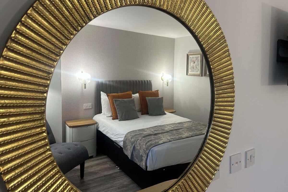 Quarto com cama, mesas de cabeceira, um banco e televisão na parede.