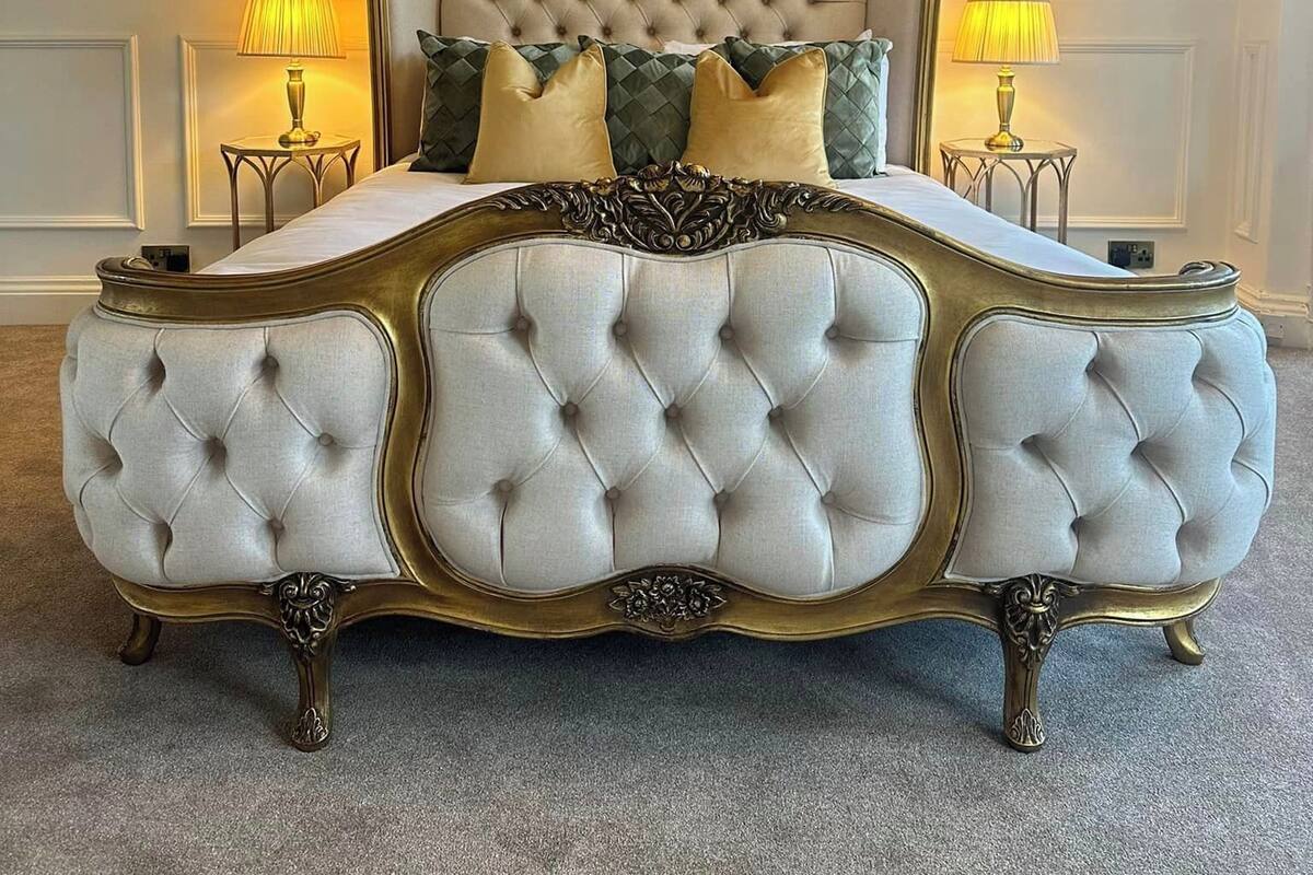 Uma cama grande e requintada com cabeceira e peseira estofadas, acompanhada por duas mesas de cabeceira com abajures.