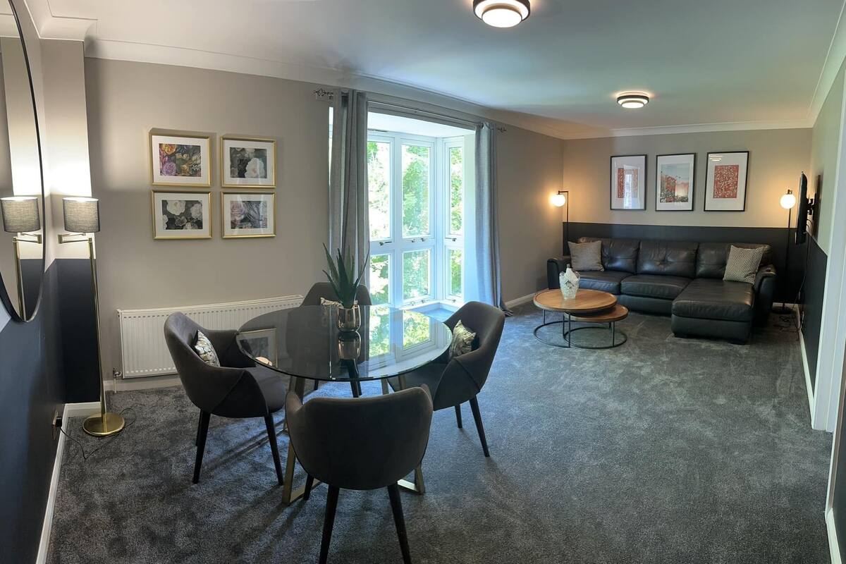 Uma sala de estar moderna com uma mesa de jantar de vidro, sofás escuros e obras de arte emolduradas nas paredes.