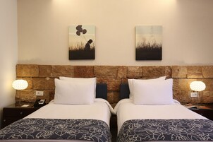 Quarto de hotel com duas camas, cabeceira de pedra e obras de arte na parede.