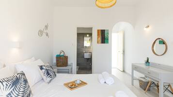Quarto de hotel com cama, mesa de cabeceira com cesta, escrivaninha com espelho e vista para o banheiro.