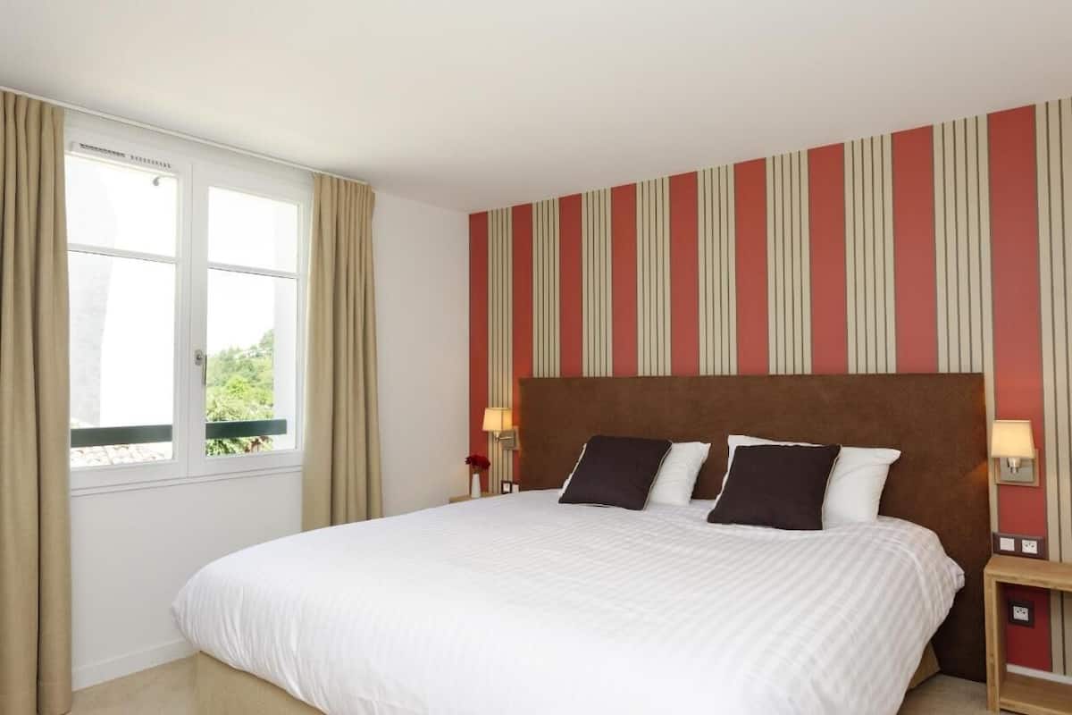 Quarto de hotel com uma cama grande, papel de parede listrado e uma janela com cortinas.