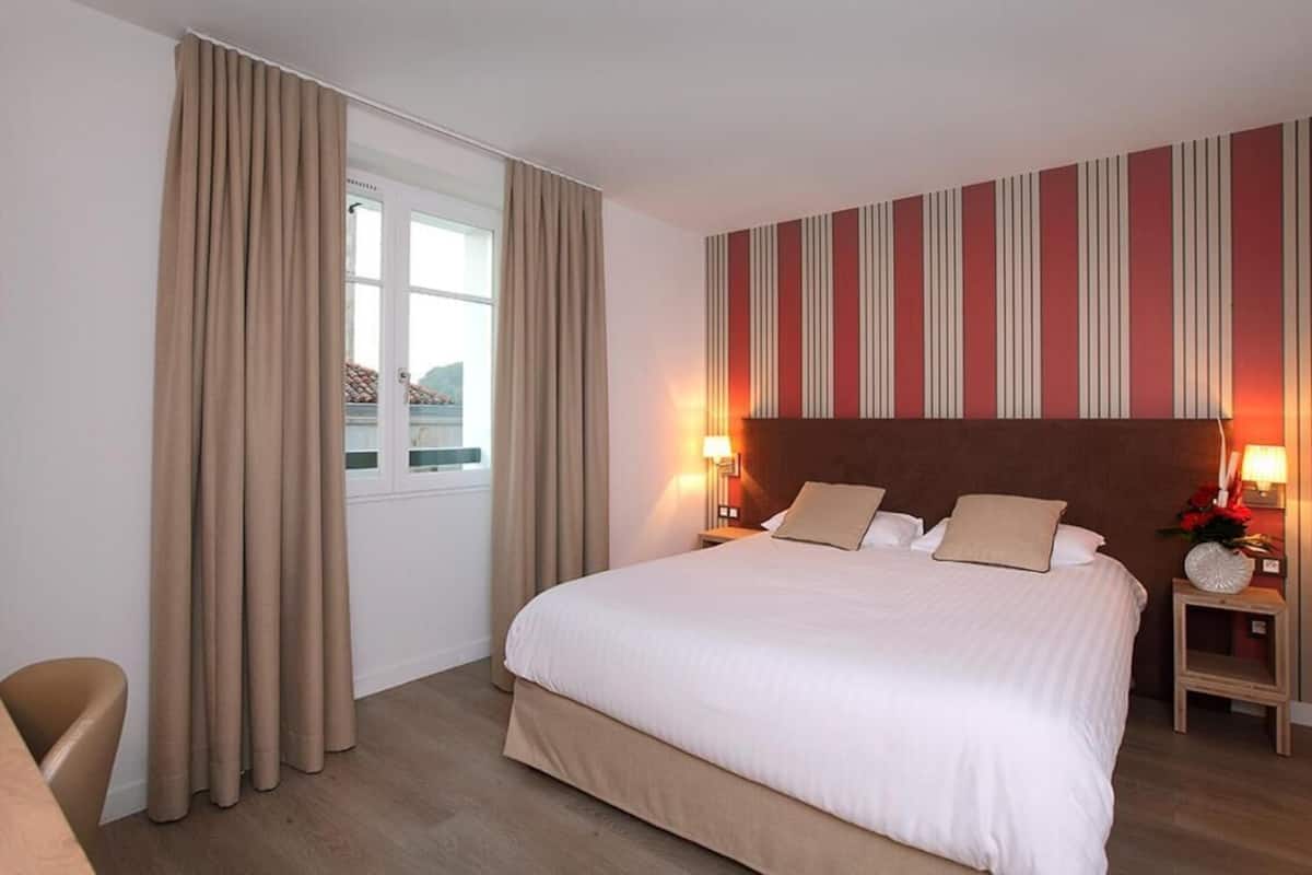 Quarto de hotel com uma cama grande, duas mesas de cabeceira com luminárias, uma janela com cortinas e uma parede listrada.