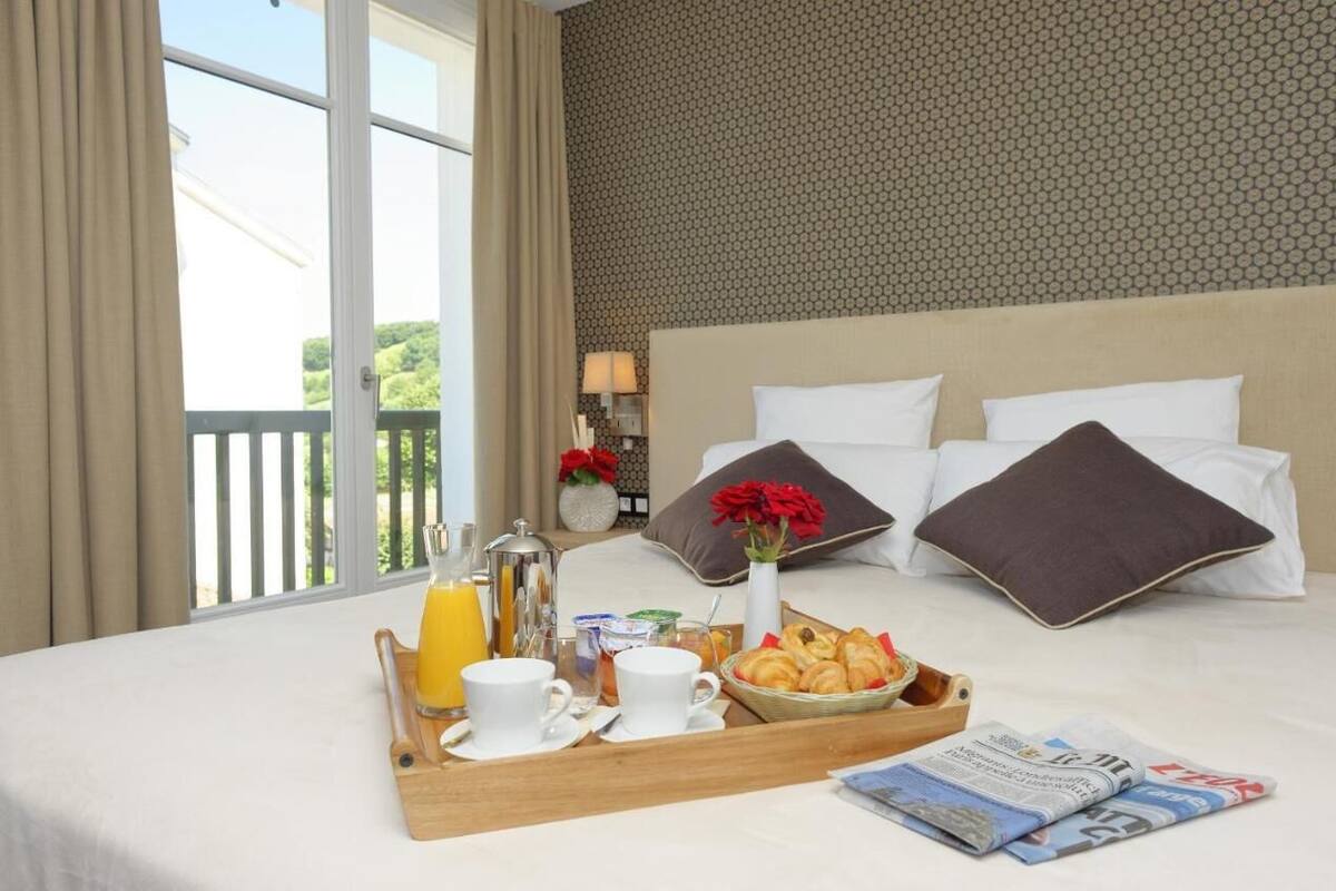 Quarto de hotel com cama, bandeja de café da manhã e vista para o verde lá fora.