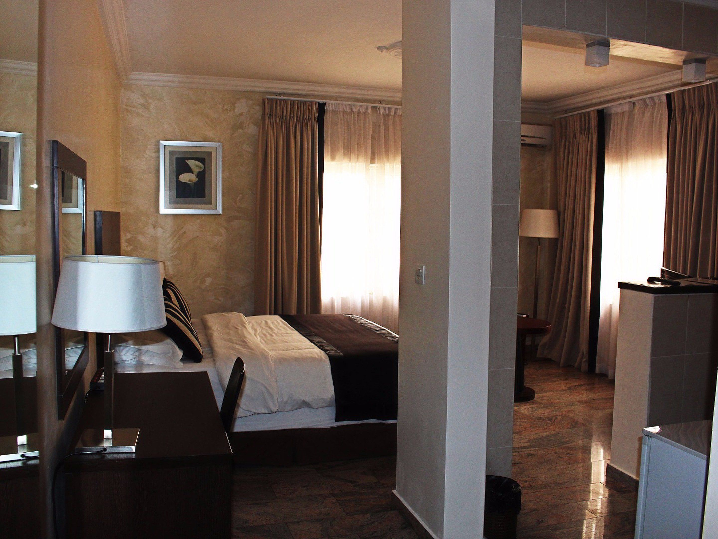 Quarto de hotel com cama, escrivaninha, cadeira, luminária e espelho.