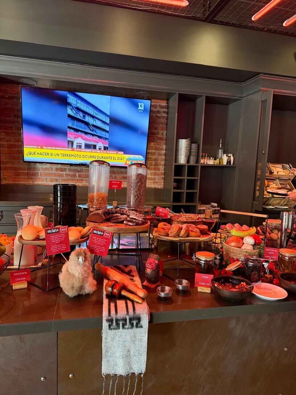 Uma mesa de buffet com diversos alimentos e uma televisão exibindo um noticiário.