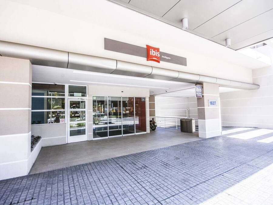 Entrada moderna de hotel com portas de vidro, placa indicando 'ibis Hotel Antofagasta' e sinalização para 'cozinha'.