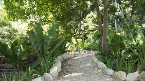 Uma trilha de cascalho ladeada por pedras grandes e vegetação exuberante, serpenteando por um jardim.