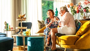 Quarto com um sofá amarelo, uma poltrona azul e uma mesinha redonda com um objeto decorativo.
