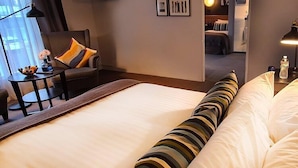 Quarto de hotel com uma cama grande, uma escrivaninha com cadeira, uma TV na parede e quadros decorativos.