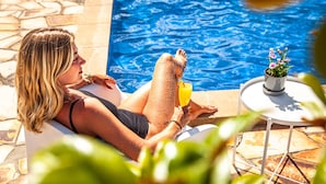 Uma pessoa relaxando à beira da piscina, com uma bebida e um vaso de planta por perto.