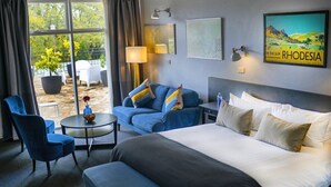 Quarto de hotel com uma cama grande, um sofá azul, uma mesa redonda e vista para o exterior.