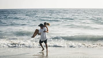 Uma cena de praia com uma pessoa carregando outra às costas, caminhando pela orla.