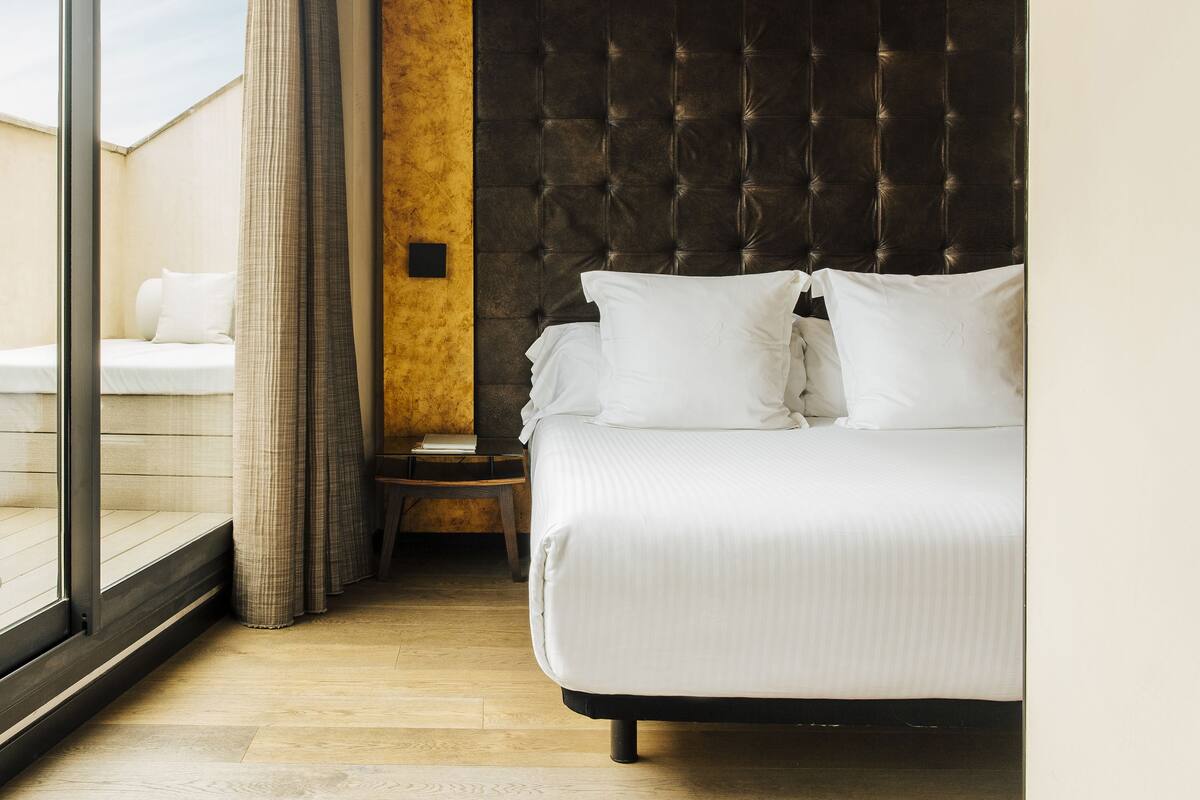 Quarto moderno com uma cama grande, cabeceira e vista do céu pela janela.