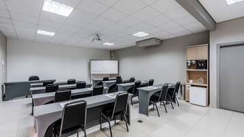 Sala de conferências com mesas, cadeiras, quadro branco e pequena cozinha.
