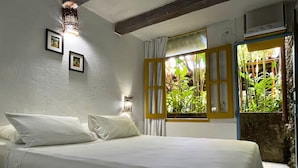 Quarto com cama, janela com persianas abertas e luminária fixada na parede.