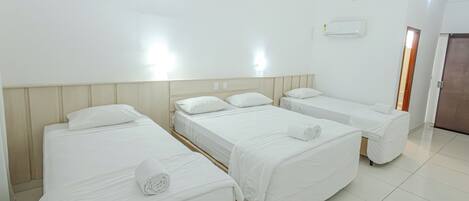 Quarto de hotel com três camas individuais, cada uma com uma toalha dobrada.