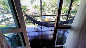 Uma rede numa varanda com vista para um parquinho e palmeiras.