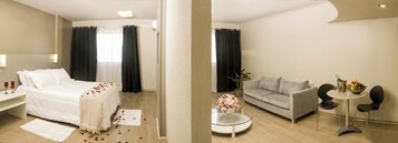 Quarto de hotel com cama, sofá, mesa de jantar e uma pequena mesa com flores.
