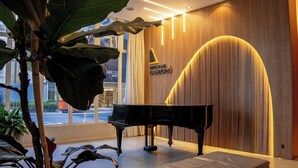 Um saguão moderno de hotel com um piano de cauda, uma parede de madeira com design curvo e grandes vasos de plantas.