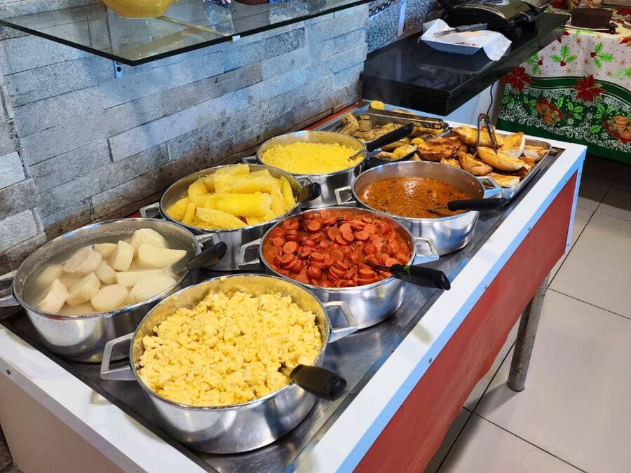 Buffet com diversos pratos, incluindo batatas, salsichas e outras opções.
