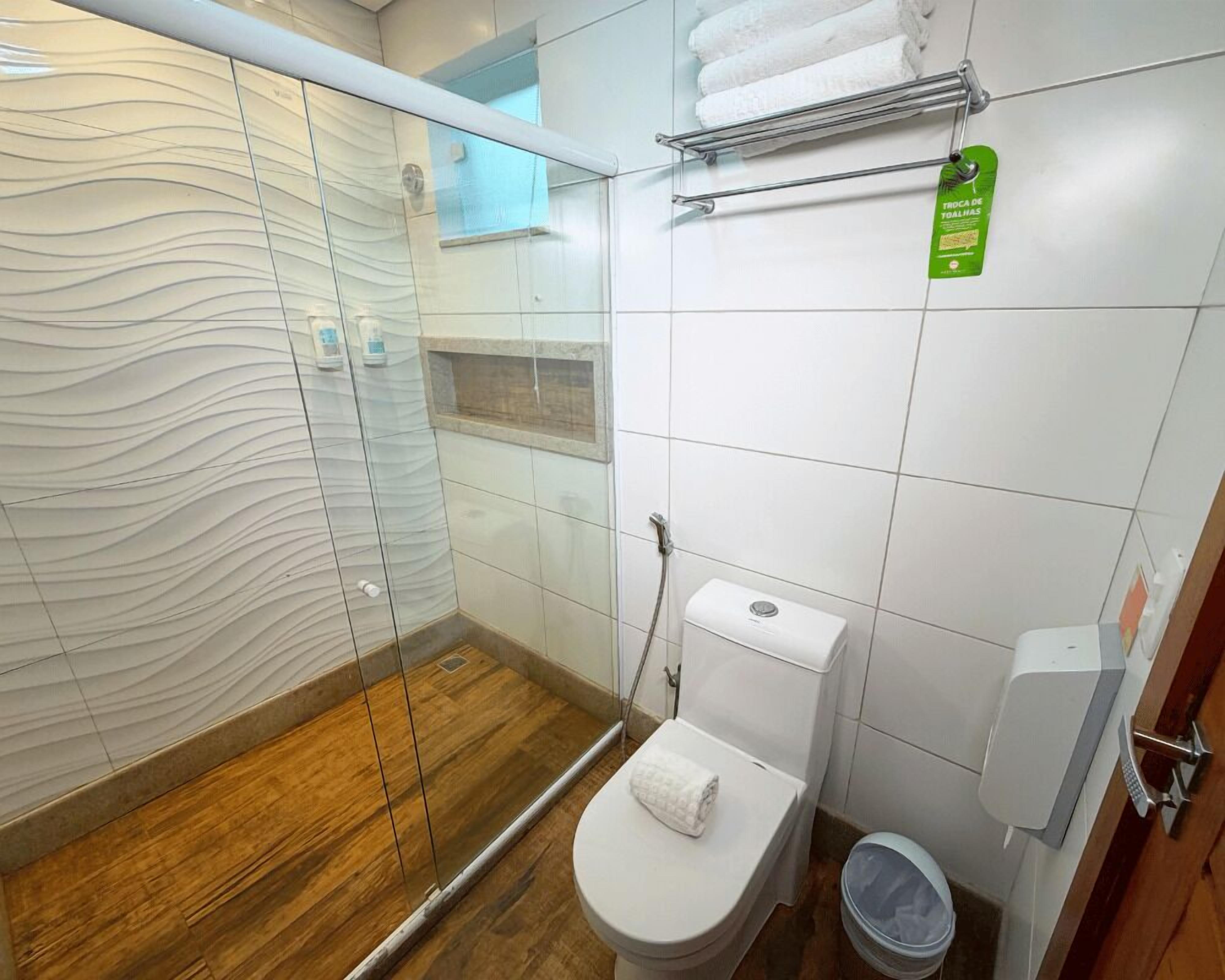 Casa de banho com cabine de duche em vidro, sanita e suporte para toalhas.