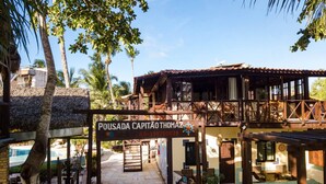 Um resort tropical com uma placa que diz "Pousada Capitao Thomaz" e um número de contato.