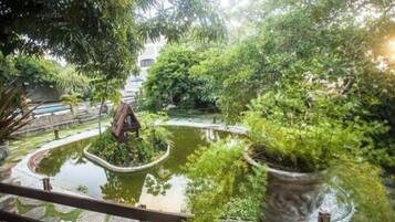 Um jardim exuberante com um lago, uma estrutura de madeira e um caminho de pedra.