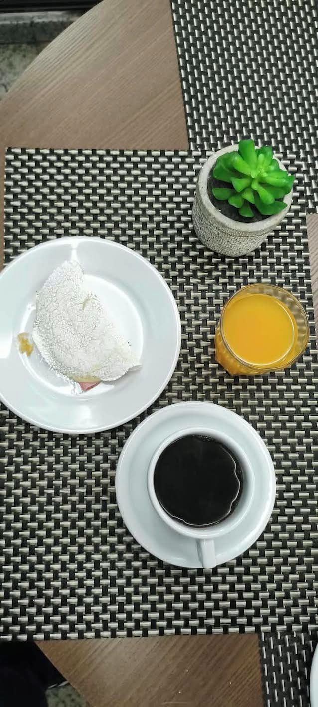 Uma mesa com um prato de comida branca, uma xícara de líquido preto e um copo de líquido amarelo.