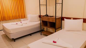 Quarto de hotel com duas camas, uma mesinha de cabeceira de madeira e uma pequena escrivaninha com cadeira.