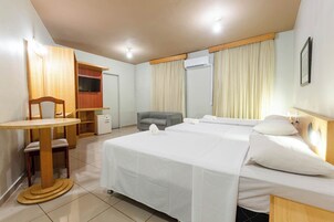 Quarto de hotel com uma cama grande, uma escrivaninha com cadeira, um frigorífico pequeno, ar condicionado e uma televisão na parede.
