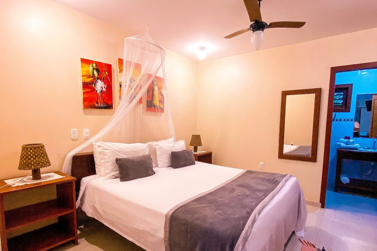 Quarto com cama, mesas de cabeceira, ventoinha no teto e obras de arte nas paredes.