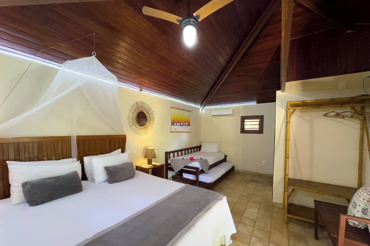 Quarto com cama, um banquinho, ventoinha no teto e janela.