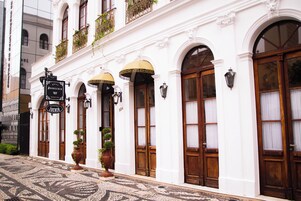 Fachada de hotel com janelas em arco, placa de identificação e plantas em vasos.