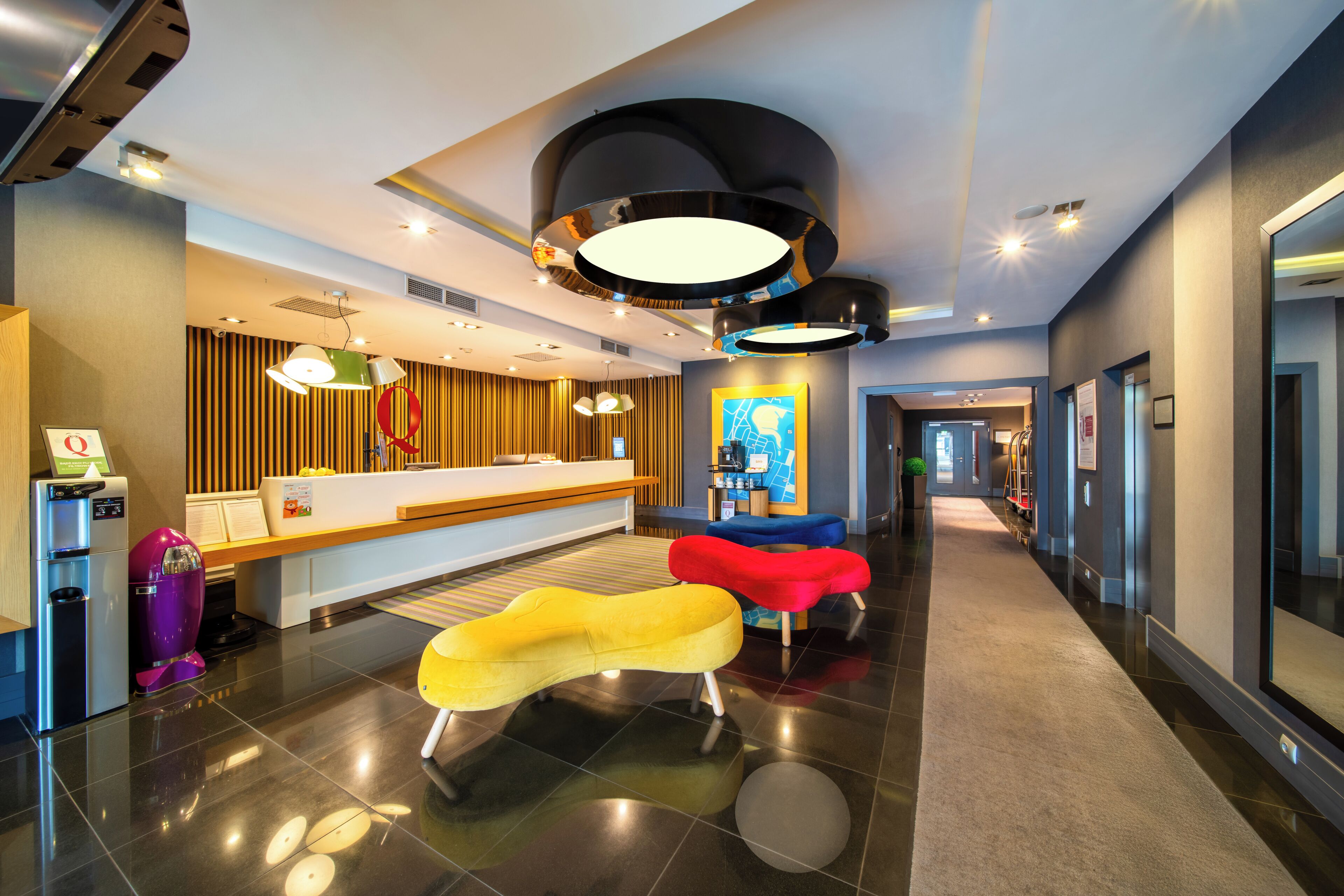 Um hall de hotel moderno com balcão de recepção, assentos coloridos e um mapa grande na parede.