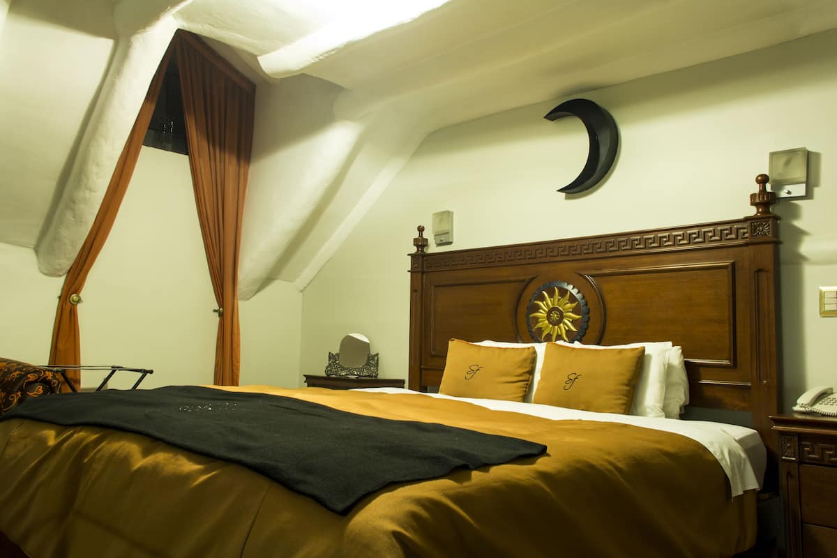 Uma cama bem arrumada com cabeceira, mesa de cabeceira com abajur e um relógio de parede.