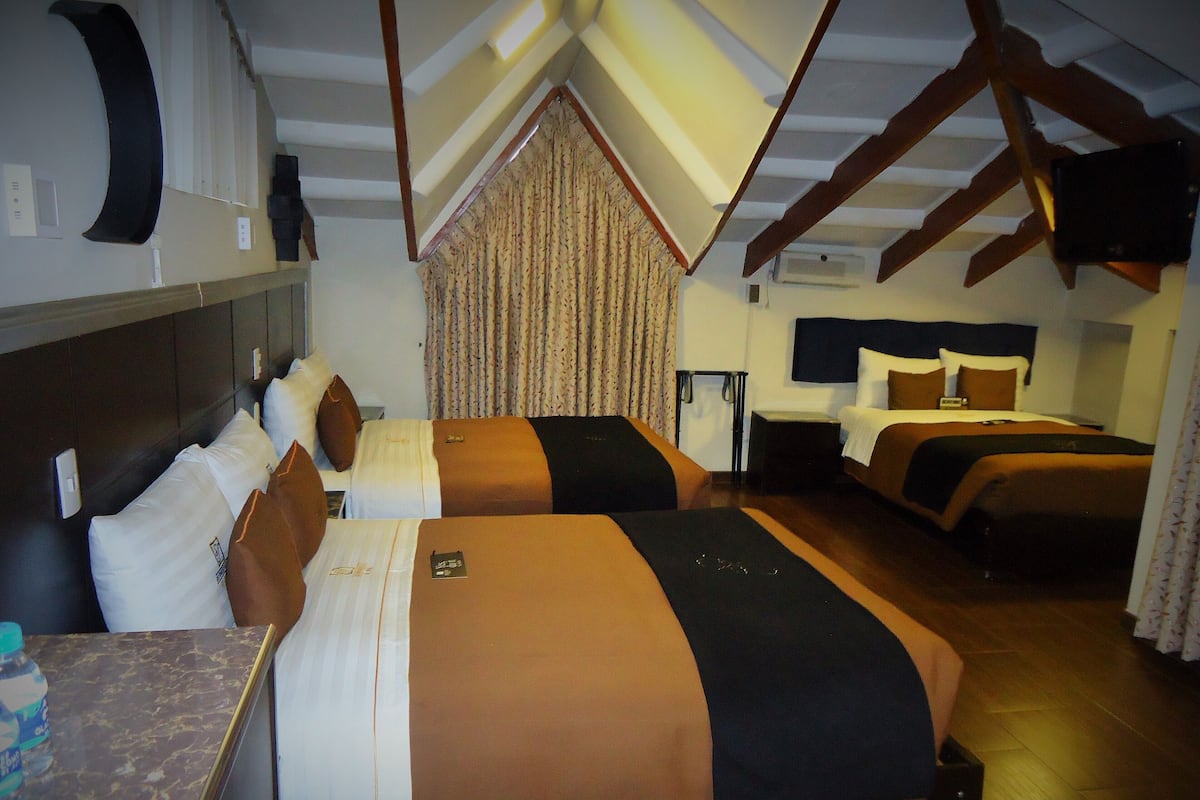 Quarto de hotel com duas camas, uma escrivaninha e um banheiro.