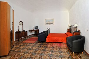 Quarto com cama, duas cadeiras, escrivaninha com computador, espelho e radiador.
