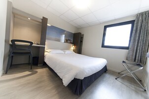 Quarto de hotel pequeno, com cama, escrivaninha e cadeira.