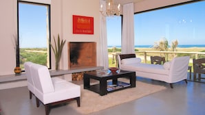 Uma sala de estar moderna com sofás brancos, lareira e vista para a praia.