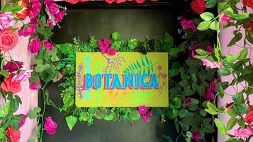 Uma porta com uma placa que diz "BOTANICA", rodeada por um arranjo floral de rosas e folhagem.