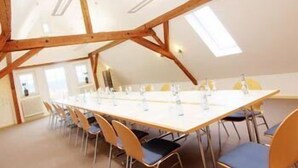Uma sala de conferências com uma mesa comprida, cadeiras e teto inclinado com vigas de madeira.
