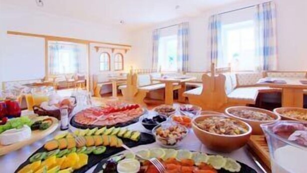 Um buffet de café da manhã com diversas frutas, legumes e carnes. Há várias mesas e cadeiras dispostas no salão.