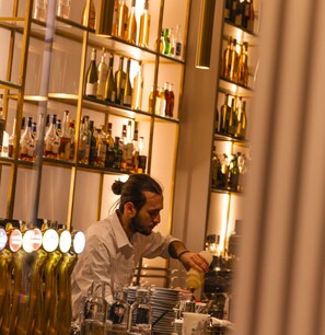 Bar com estantes de garrafas de bebidas e um bartender preparando uma bebida.