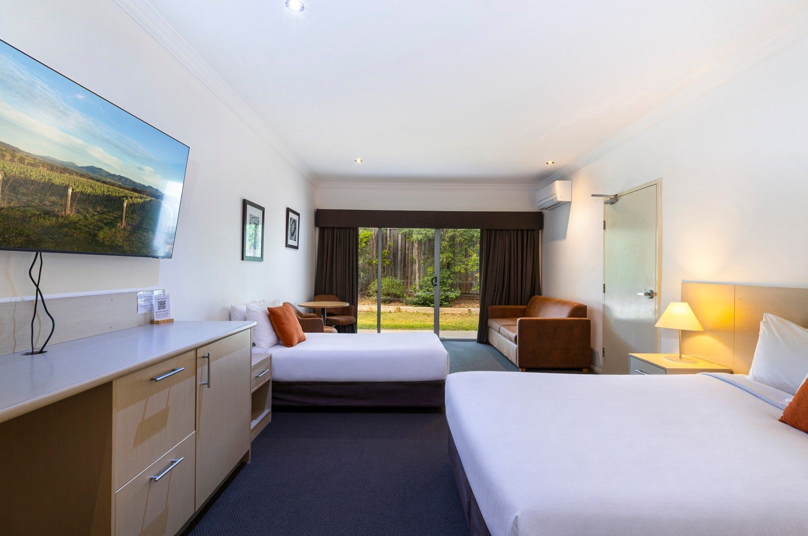 Quarto de hotel com duas camas, uma escrivaninha, uma cadeira, televisão e vista para o exterior.