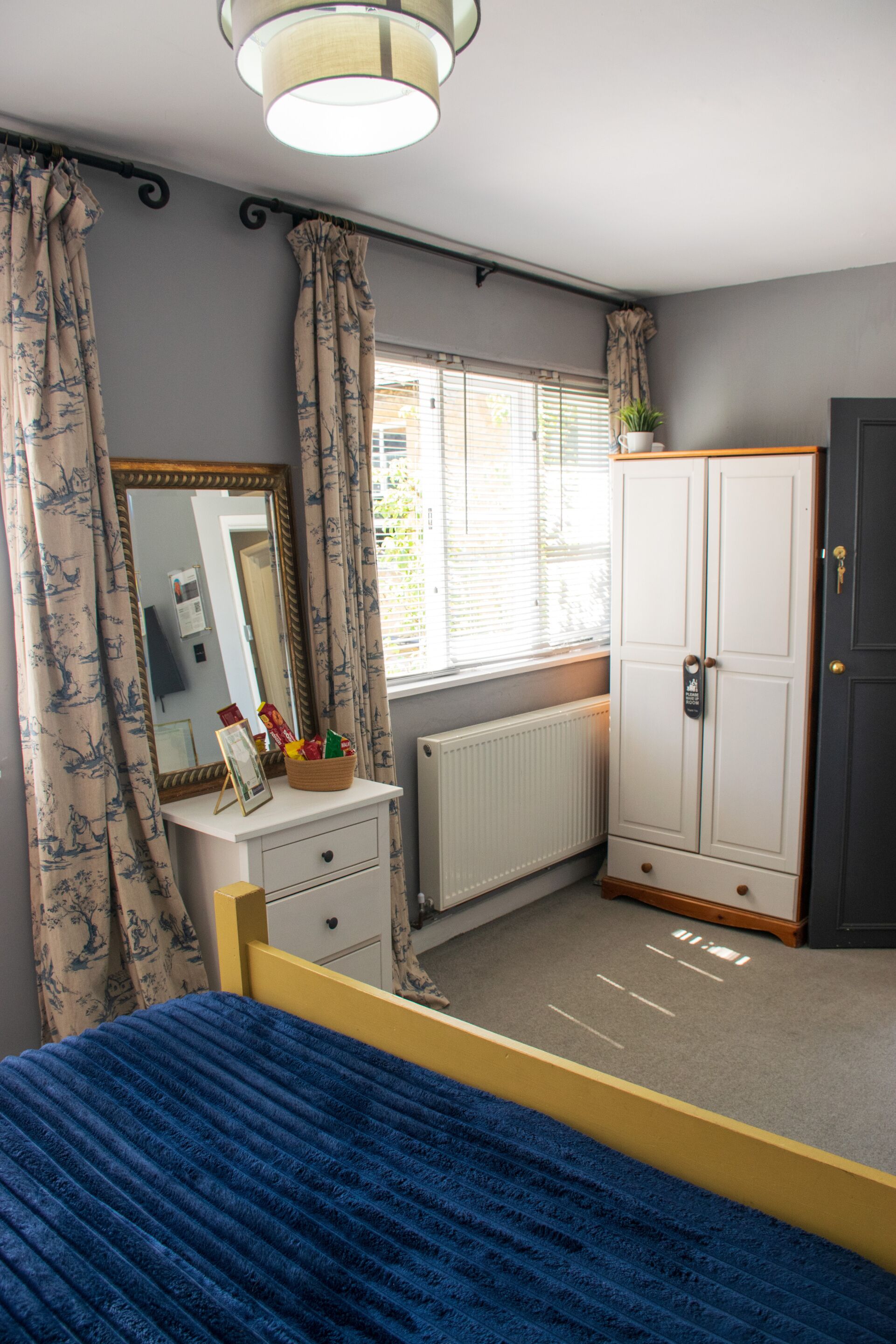 Quarto com cama, penteadeira, espelho, guarda-roupa e janela com cortinas.